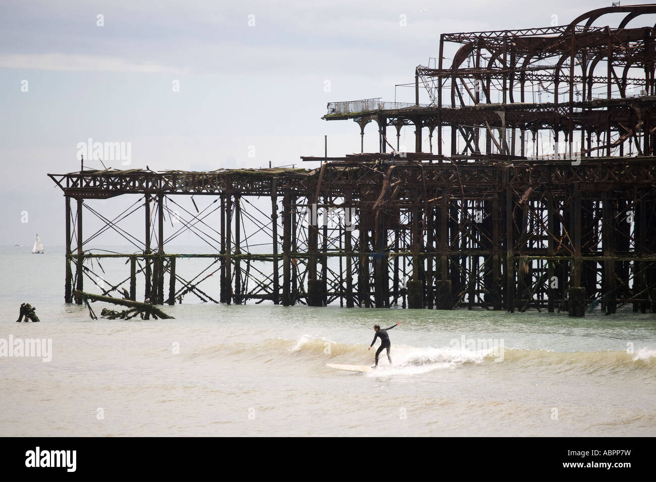Surfers ride waves along side the burned out structure of the West Pier ...