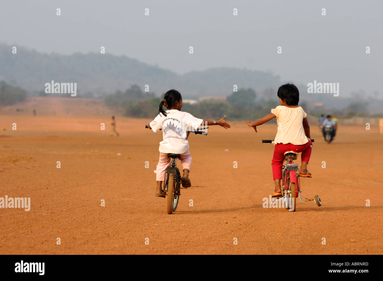 Two children reach out to hold hands while cycling along an old runway ...