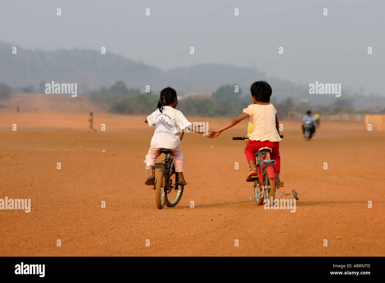 Two children reach out to hold hands while cycling along an old runway ...