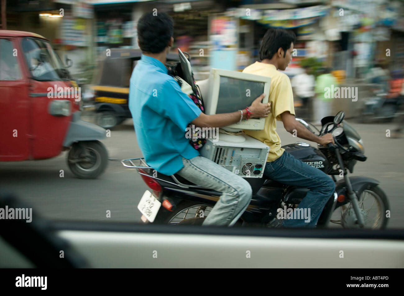 Two men carry a computer between them on the back of a motorbike ...