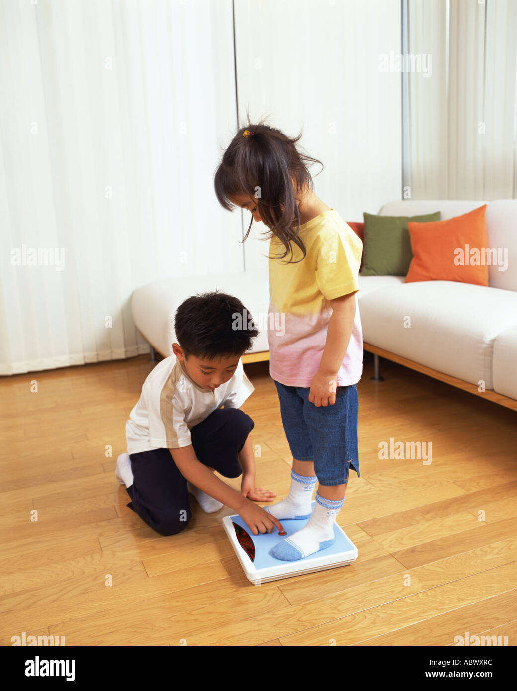 A small girl standing on scale while her brother presses button Stock ...