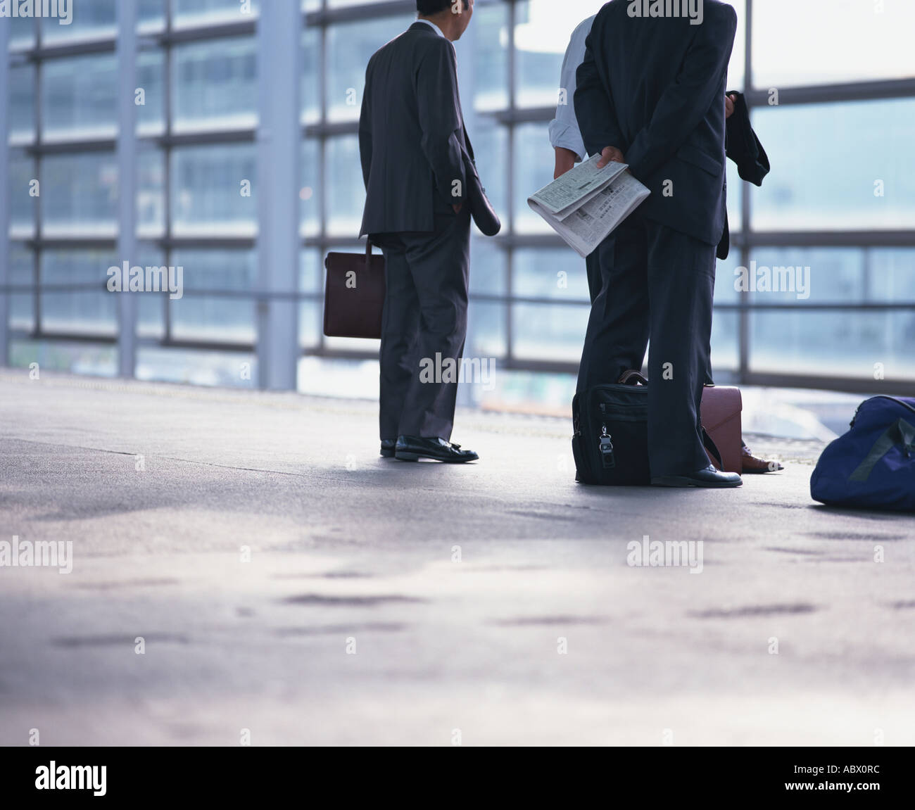 Three men in formal suit waiting on the platform with their bags and ...