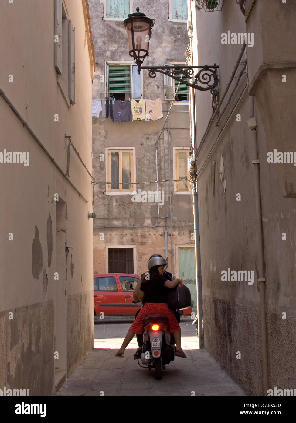 Two people riding motor scooter down narrow passageway between ...