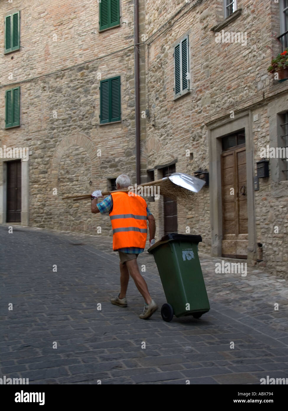 Man wearing orange safety vest carrying shovel and broom on shoulder ...