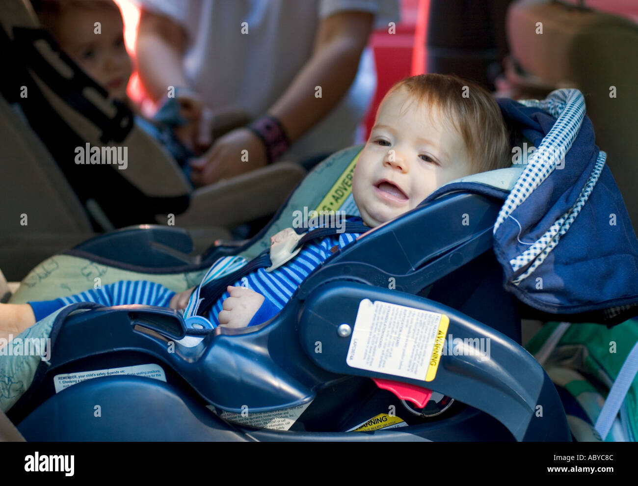 Smiling baby boy strapped into rear facing car seat with warning labels ...