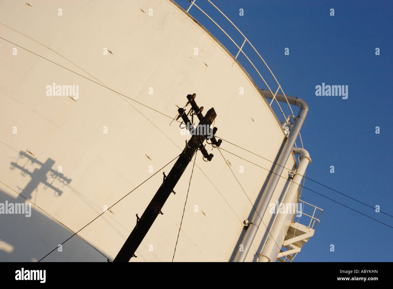 Telegraph pole and wires silhouetted against a storage tank at Kerry ...