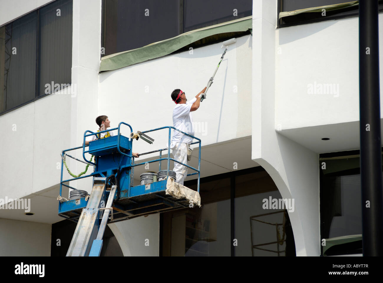 Painters on a rented portable elevator lift paint the exterior of ...