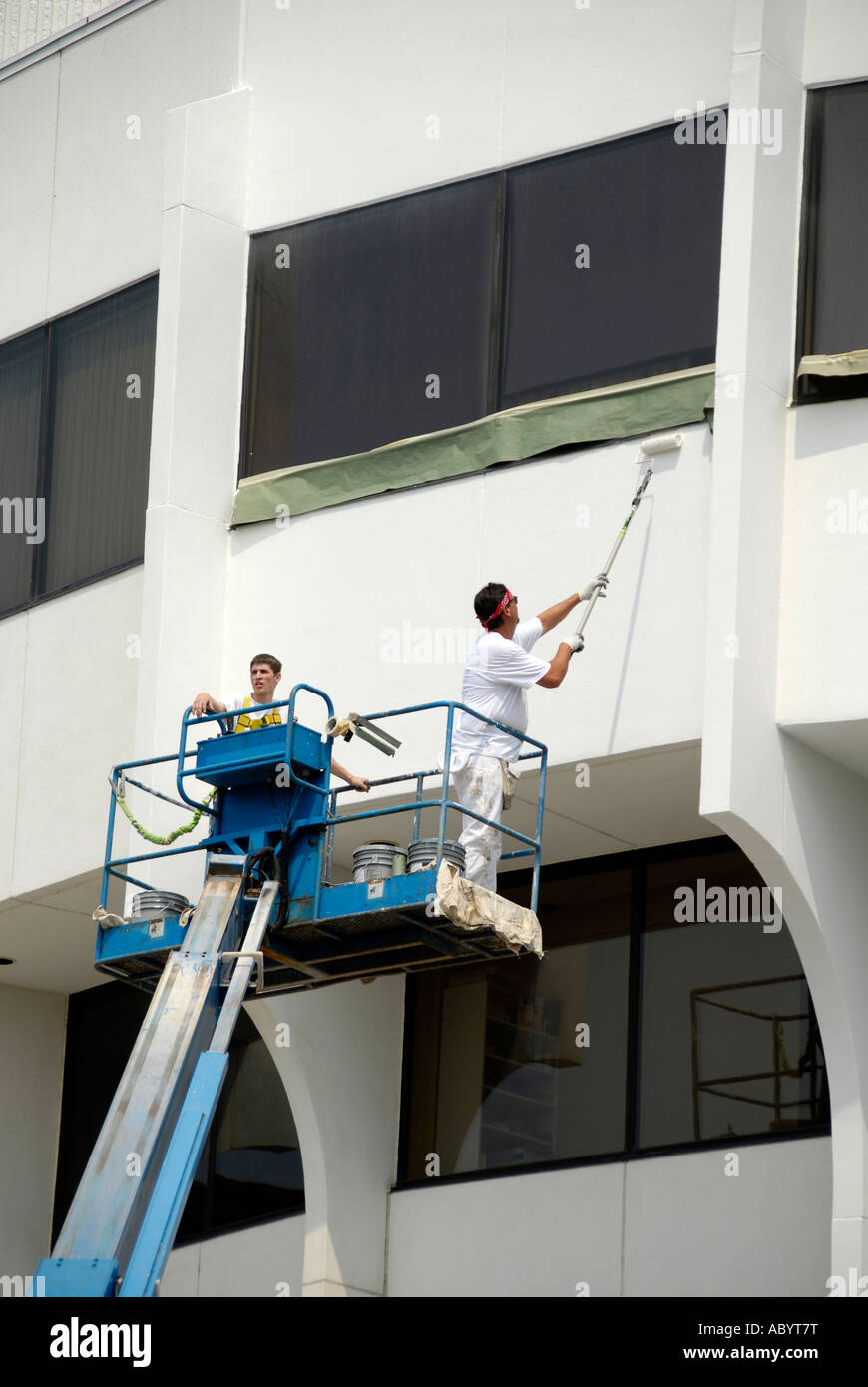 Painters on a rented portable elevator lift paint the exterior of ...