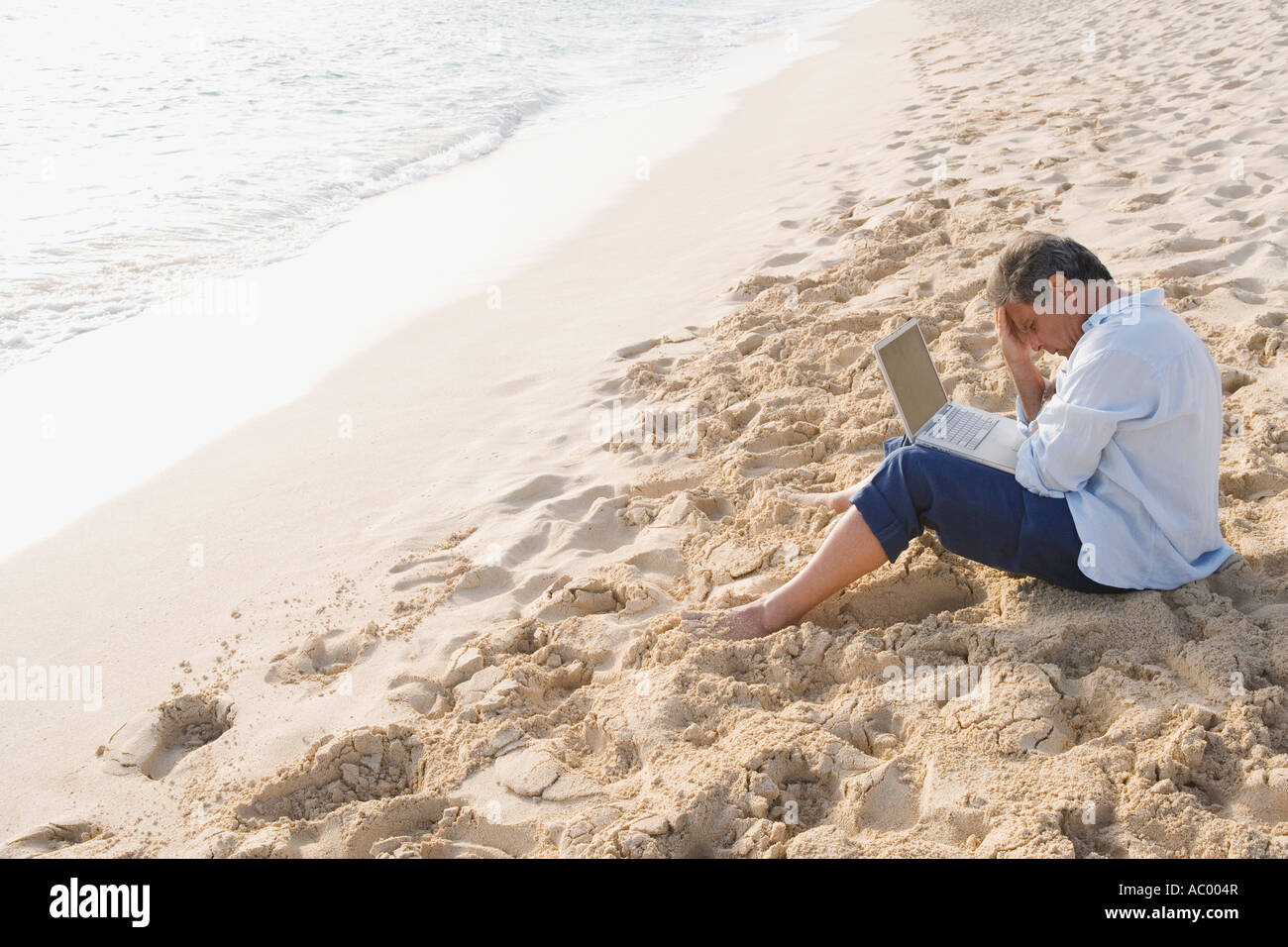 Dejected man using laptop on beach Stock Photo - Alamy