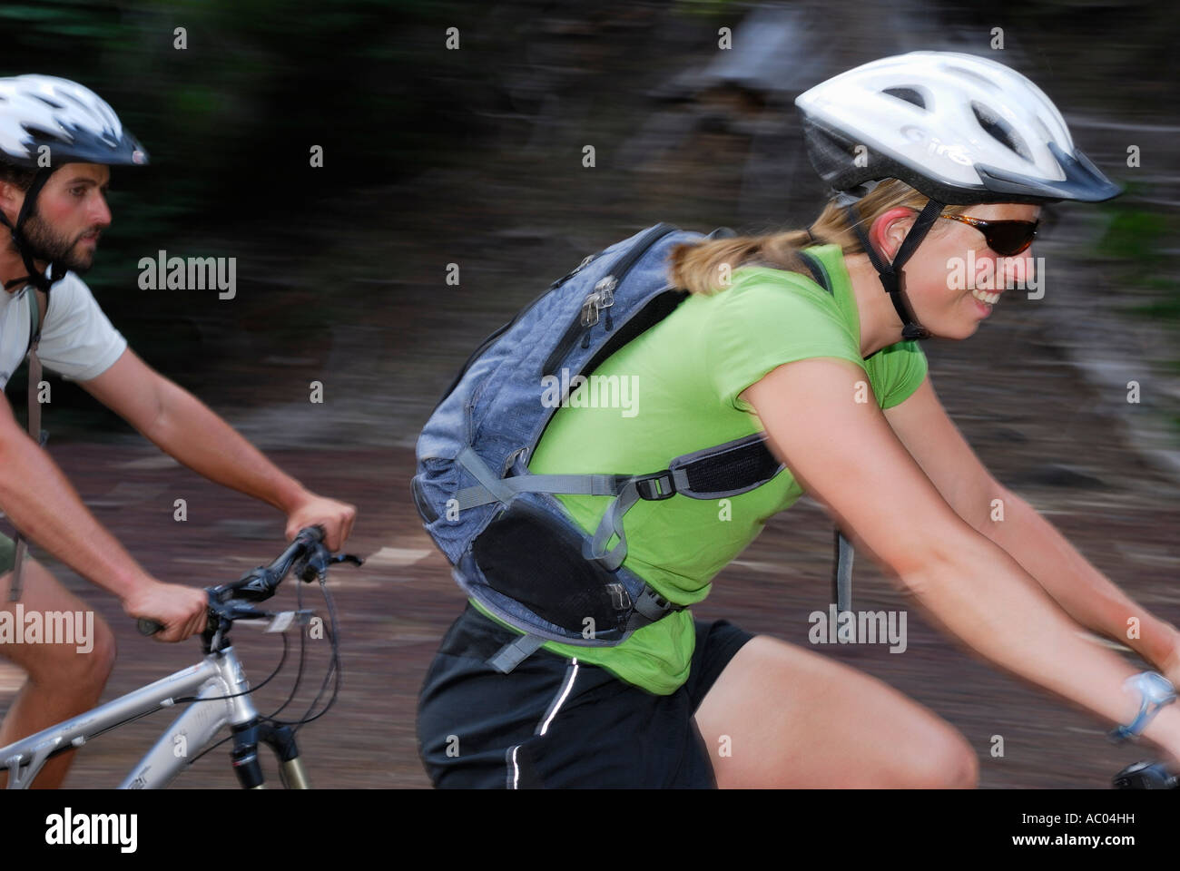 Smiling female and mae mountain bikers racing down a forest trail with ...