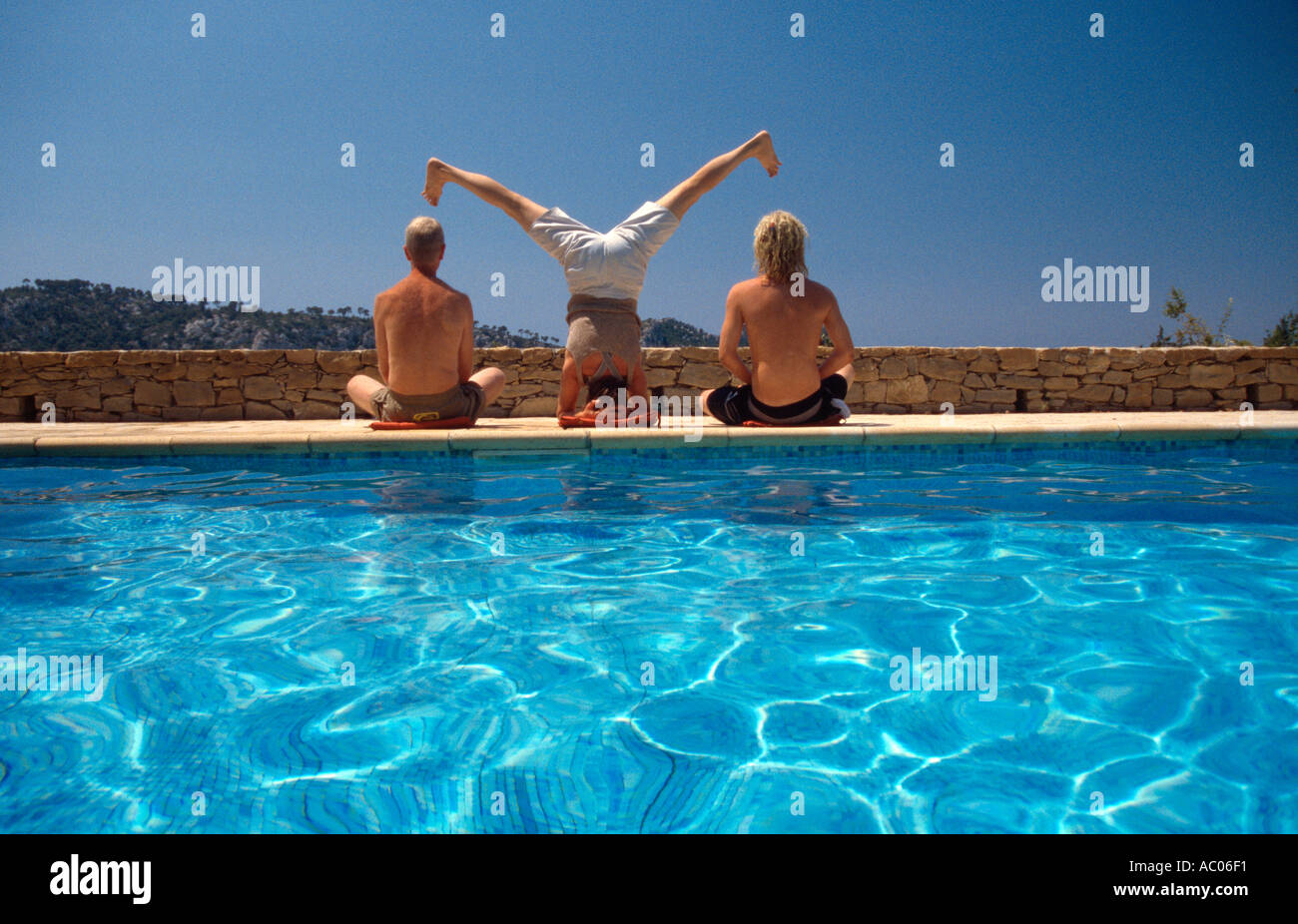 Three adults doing yoga poses asanas beside a swimming pool Stock Photo ...