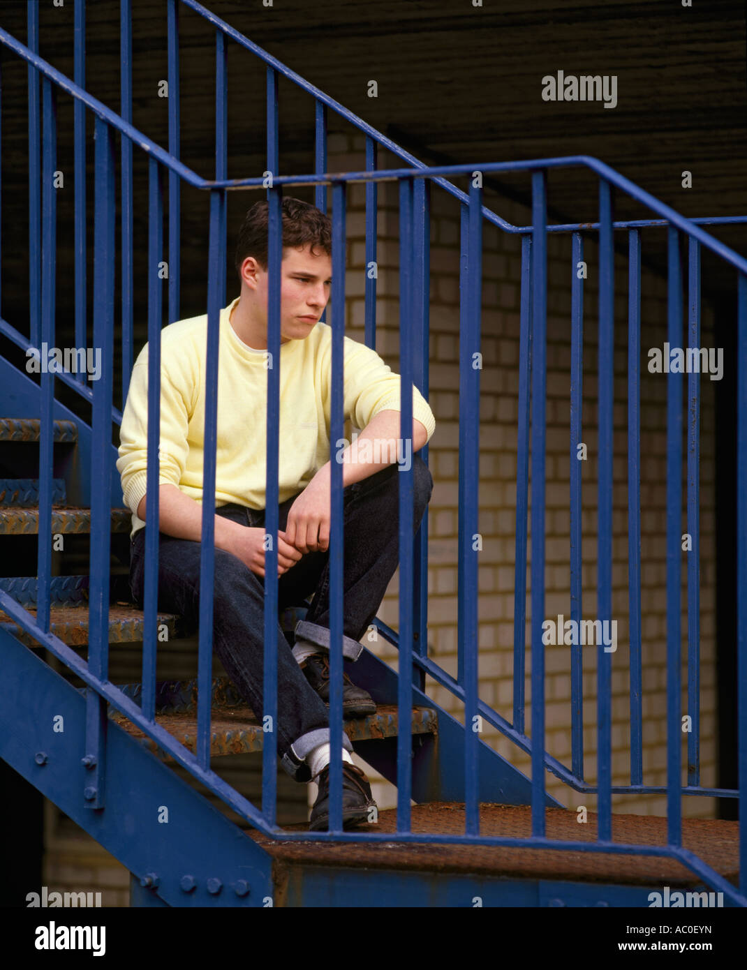 Teenage boy sitting on steps behind railings Stock Photo - Alamy