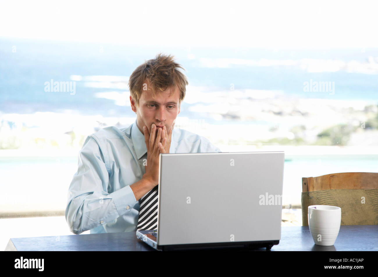 Man sitting at table, using laptop Stock Photo - Alamy