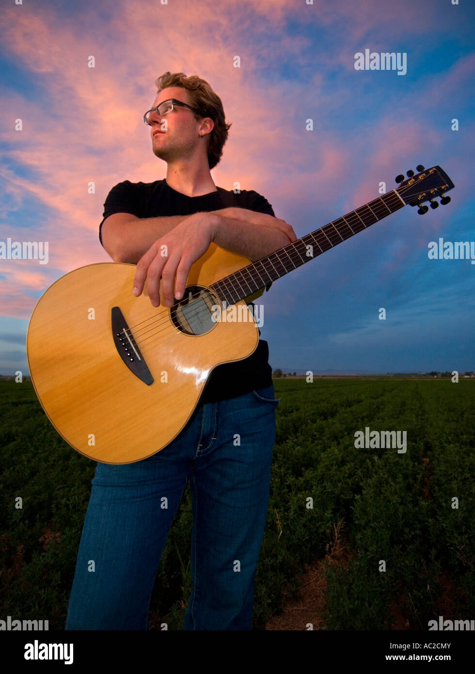 Musician Marcus Eaton at sunset in a field with guitar Stock Photo - Alamy
