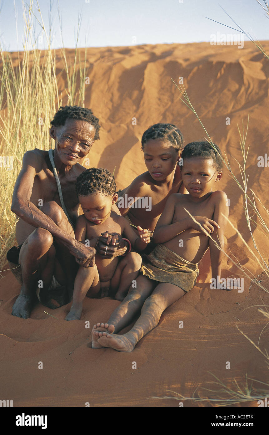 Bushman family of mother and three children sitting in sand dunes near ...