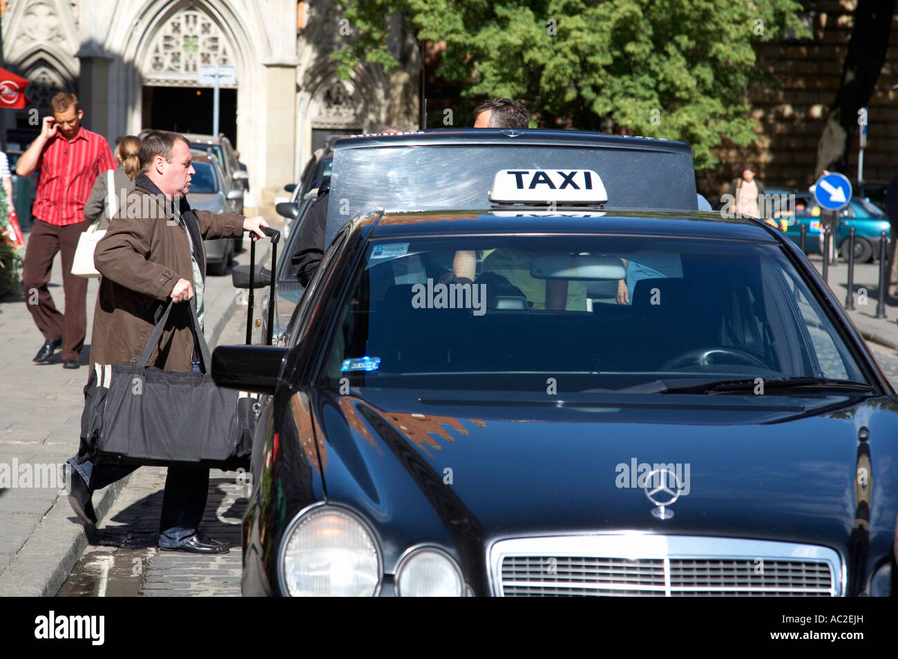 man carries luggage to open boot of a mercedes taxi cab on a rank in ...