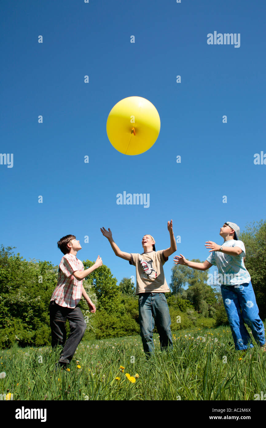 three kids trying to catch a big yellow balloon Stock Photo - Alamy