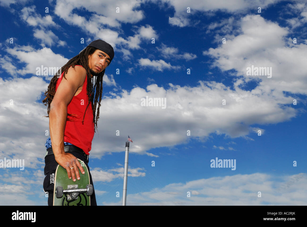 Black male skateboarder with dreadlocks posing against a blue clouded ...