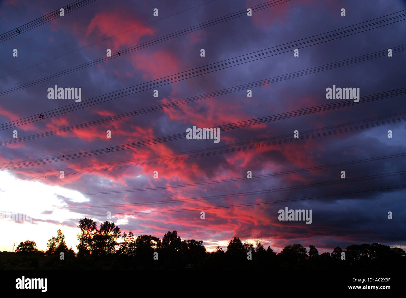 High tension hydro wires crossing a sunset with red clouds Stock Photo ...