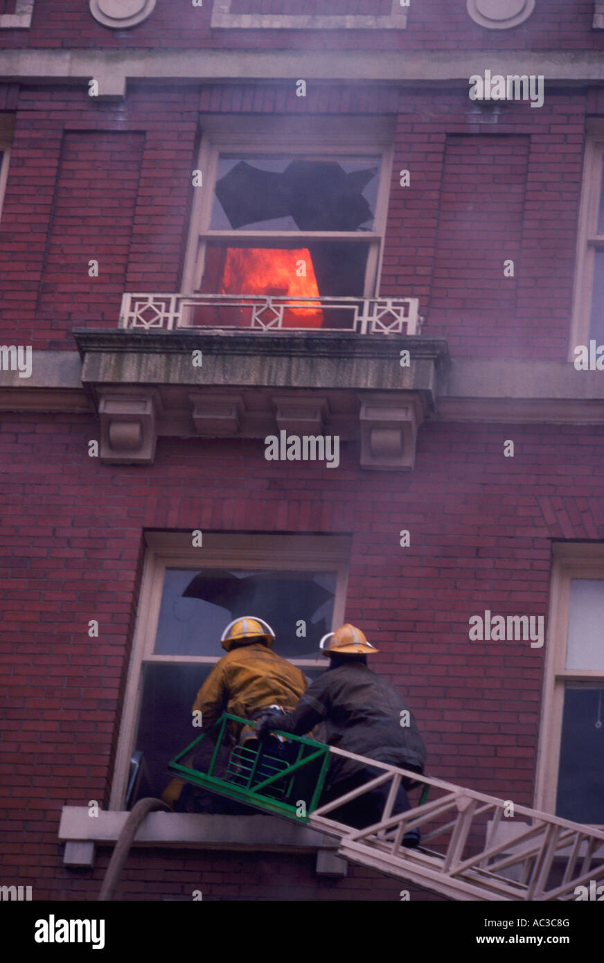 Firefighters / Firemen on Ladder fighting Fire with Hose through Broken ...