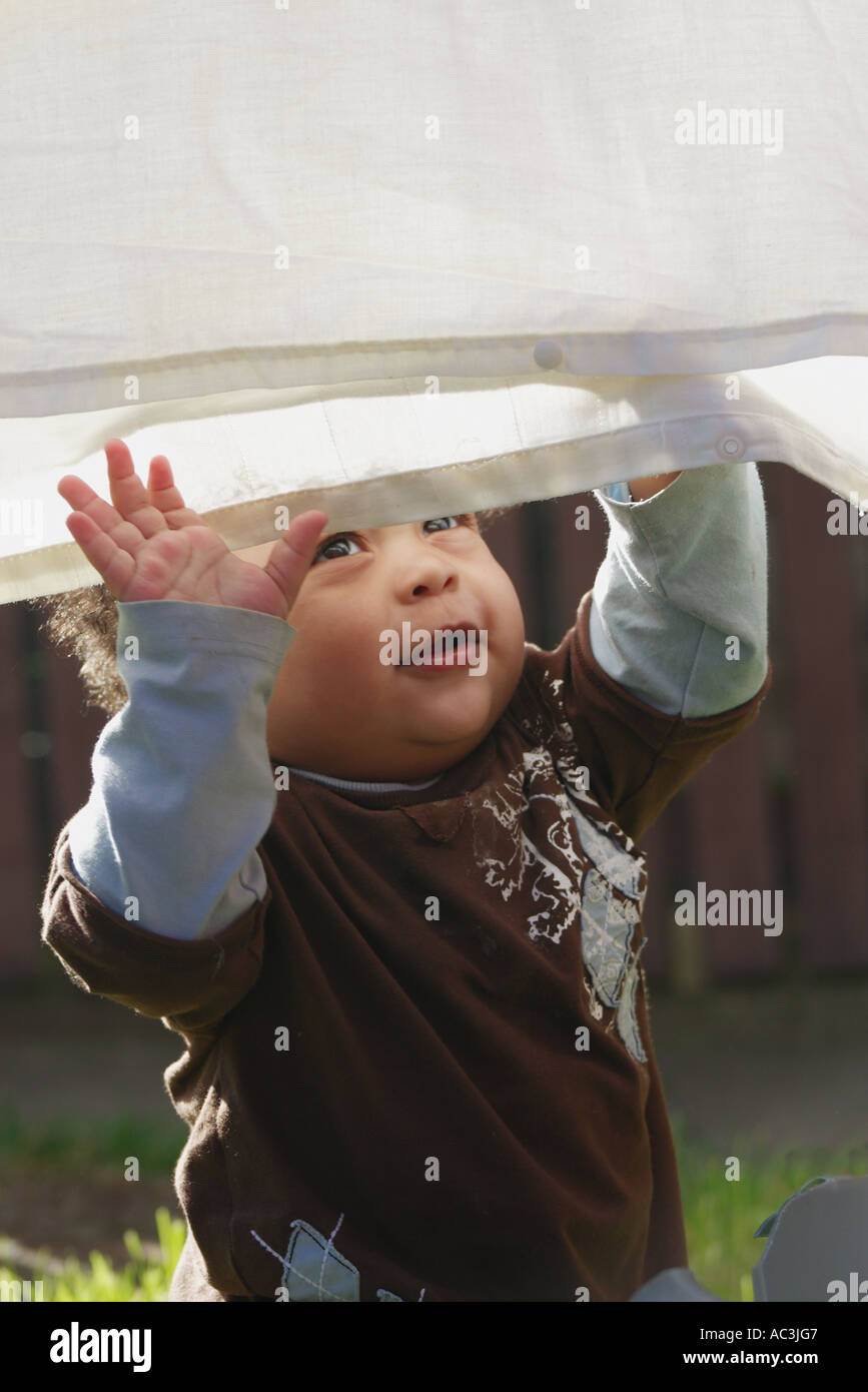 Baby boy playing with his mothers laundry on the garden washing line ...
