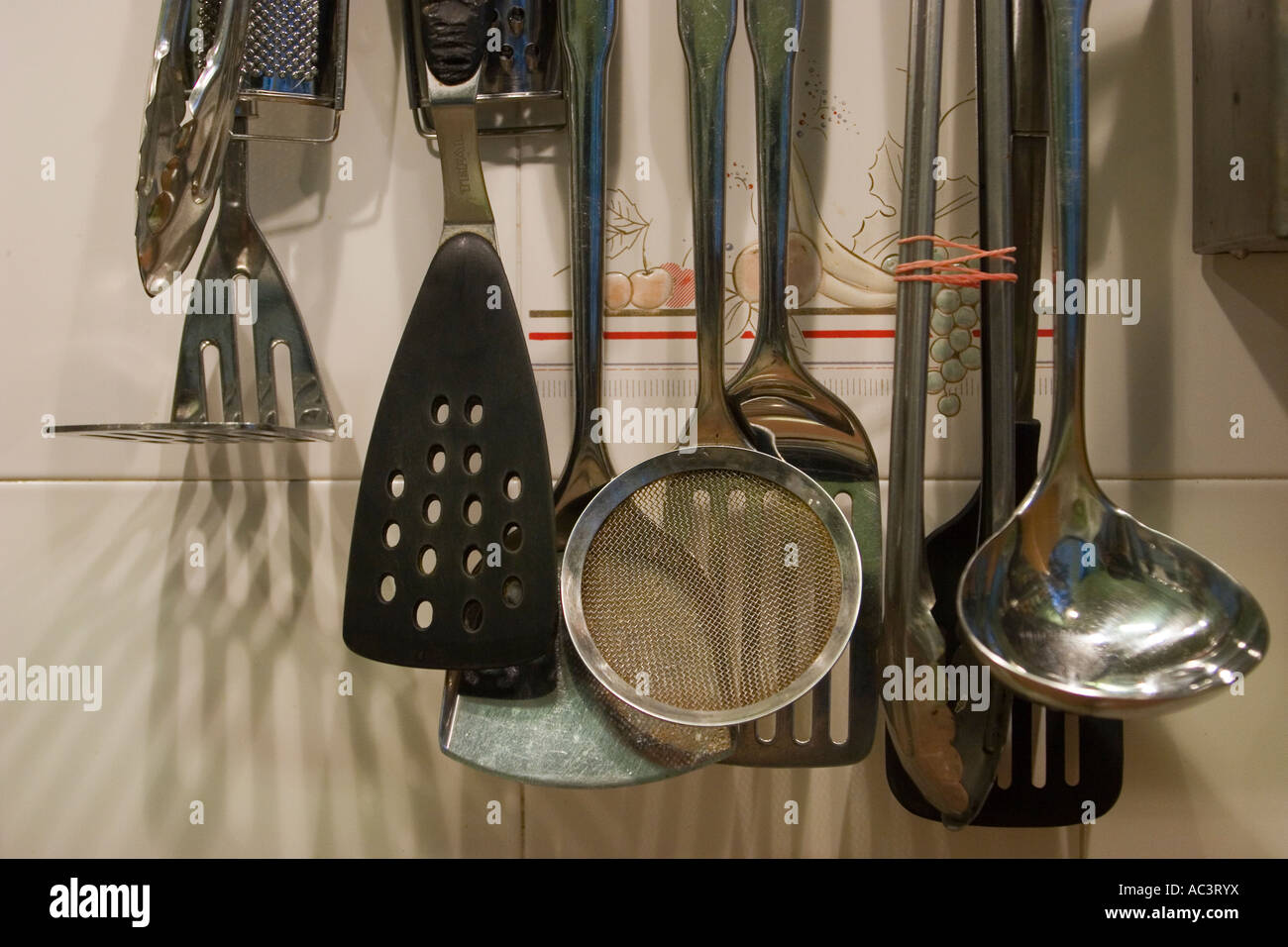 kitchen utensils hang against a tiled wall casting shadows Stock Photo ...