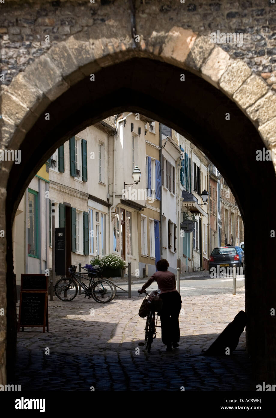 Woman cyclist in shadow pushing bicycle on cobbled road through Nevers ...