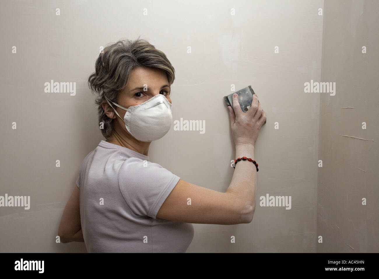 A young woman sanding down the plaster of a wall (France). Jeune femme ...