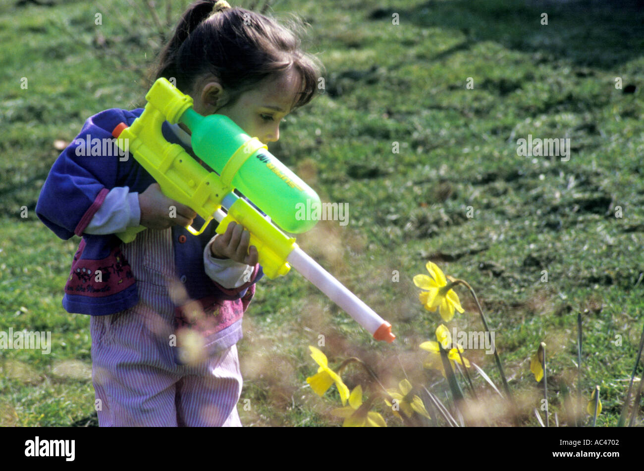 3 year old girl watering flowers with plastic water cannon gun Stock ...