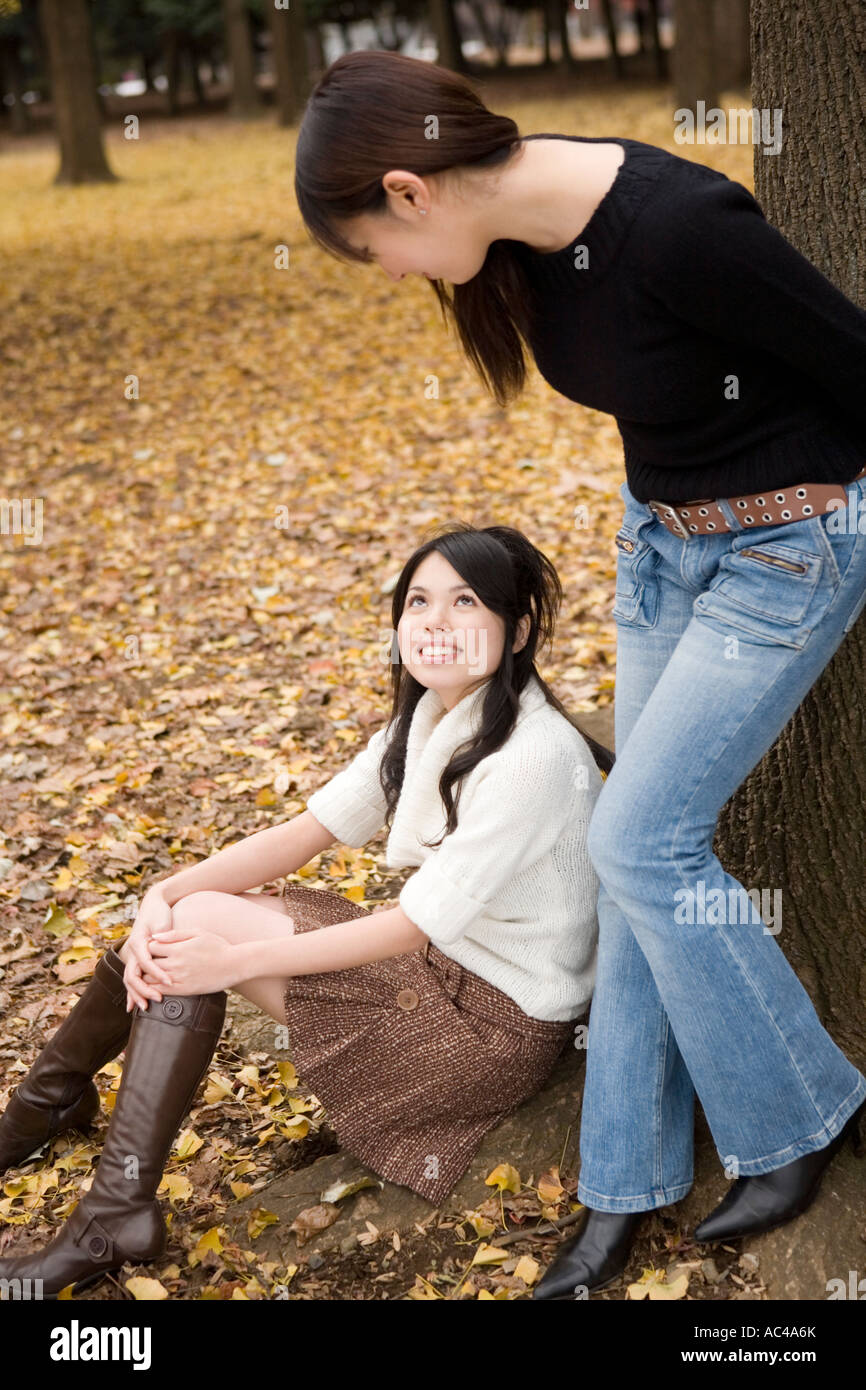 Two young women talking by tree Stock Photo - Alamy