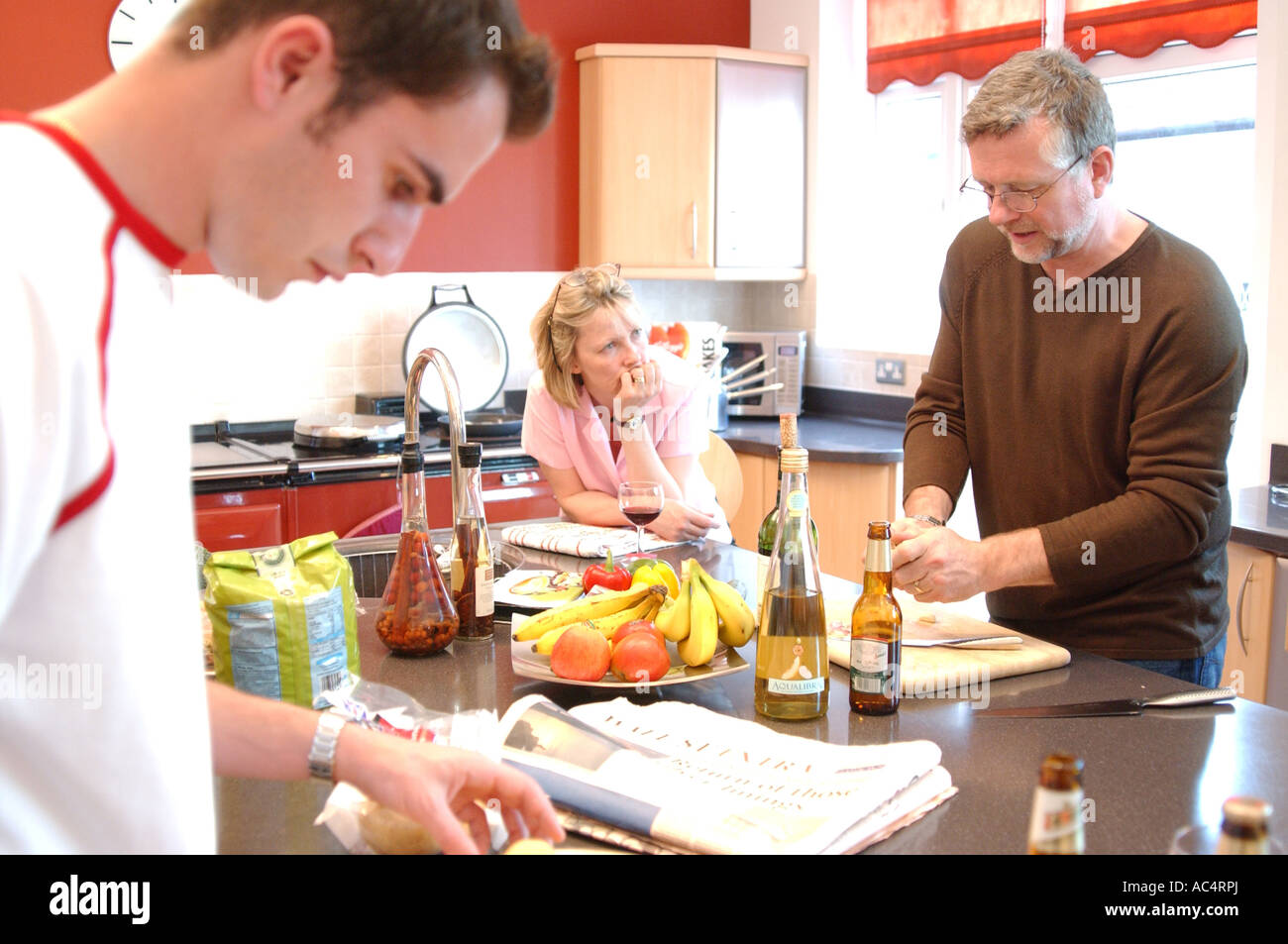 British family in kitchen at home making lunch together and chatting in ...