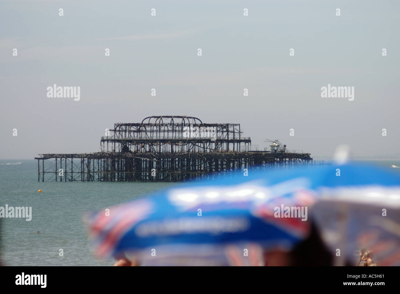 burned out shell of Brighton west pier and blue parasol in foreground ...