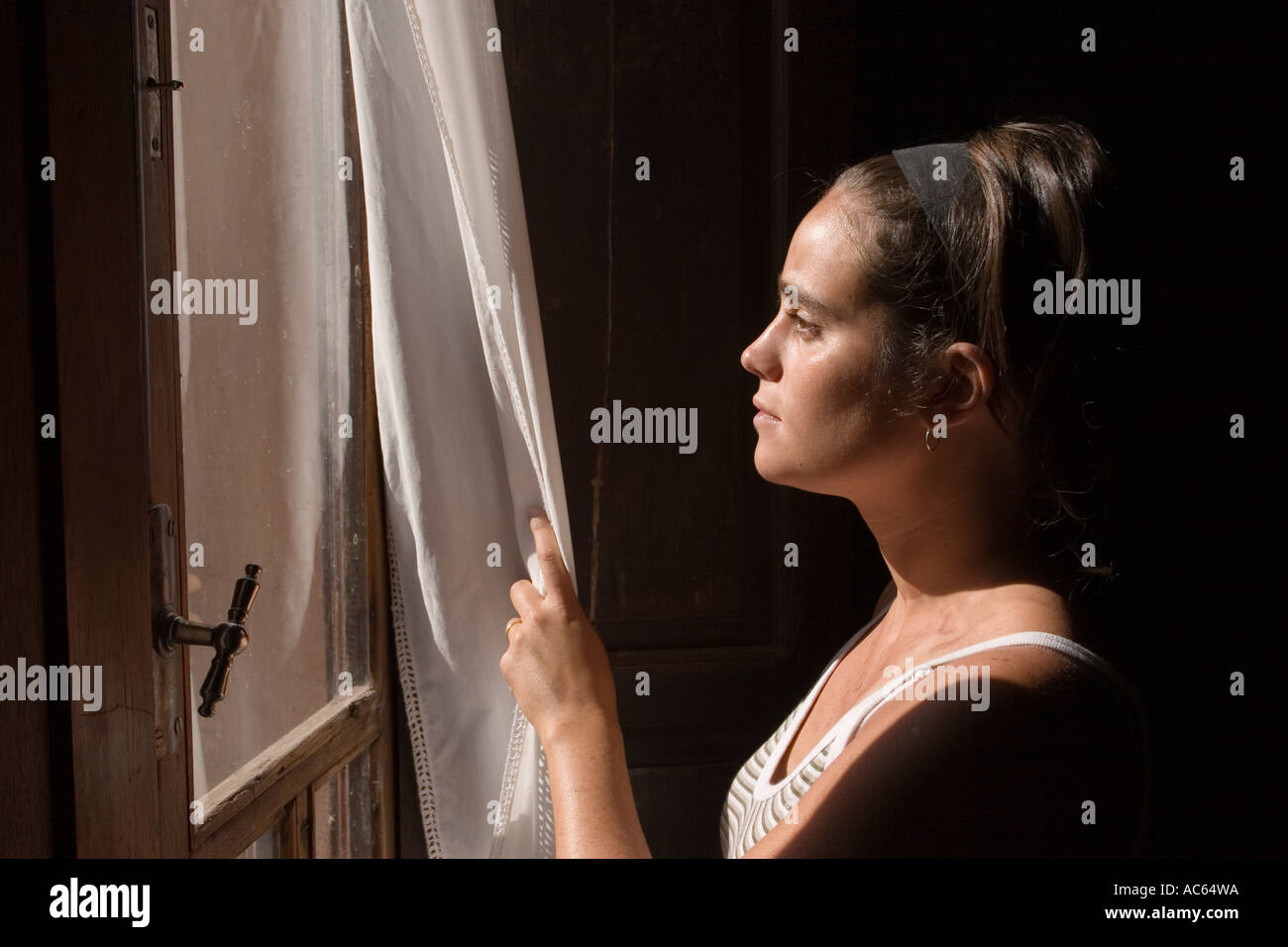 WOMAN LOOKING THROUGH A WINDOW IN DARK ROOM Woman looking through an ...