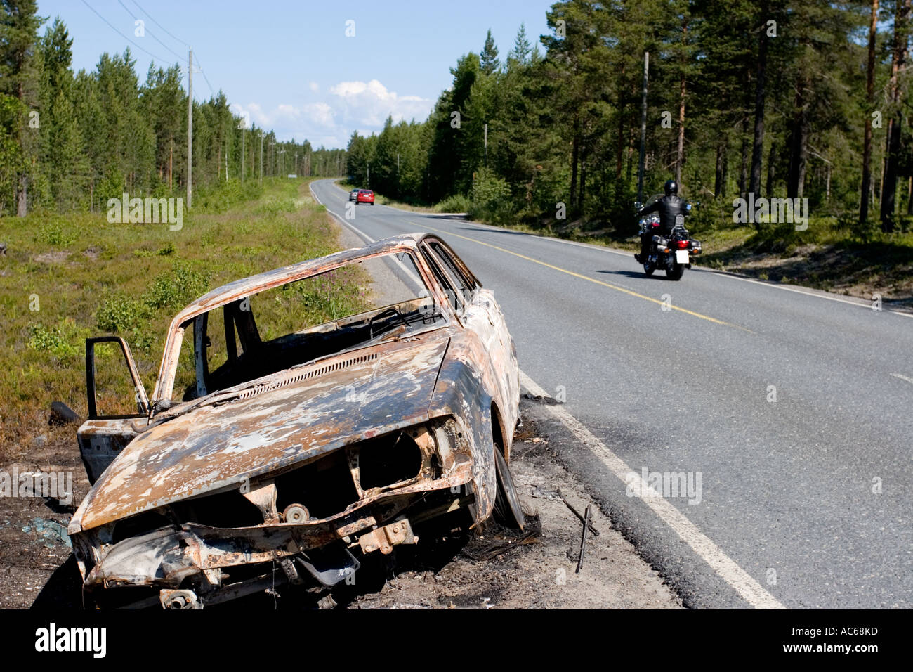Burned Volvo sedan at country road . Motorcyclist and cars passing by ...