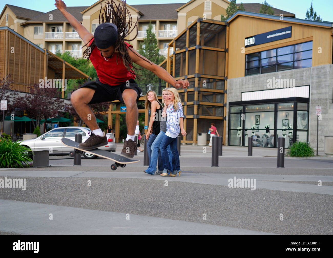 Three girls razzing an airborne Black male skateboarder with dreadlocks ...