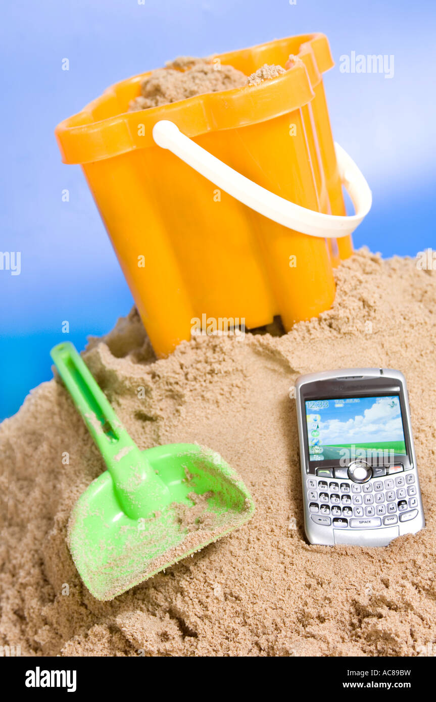a blackberry mobile phone on the beach with sand and a bucket and spade ...