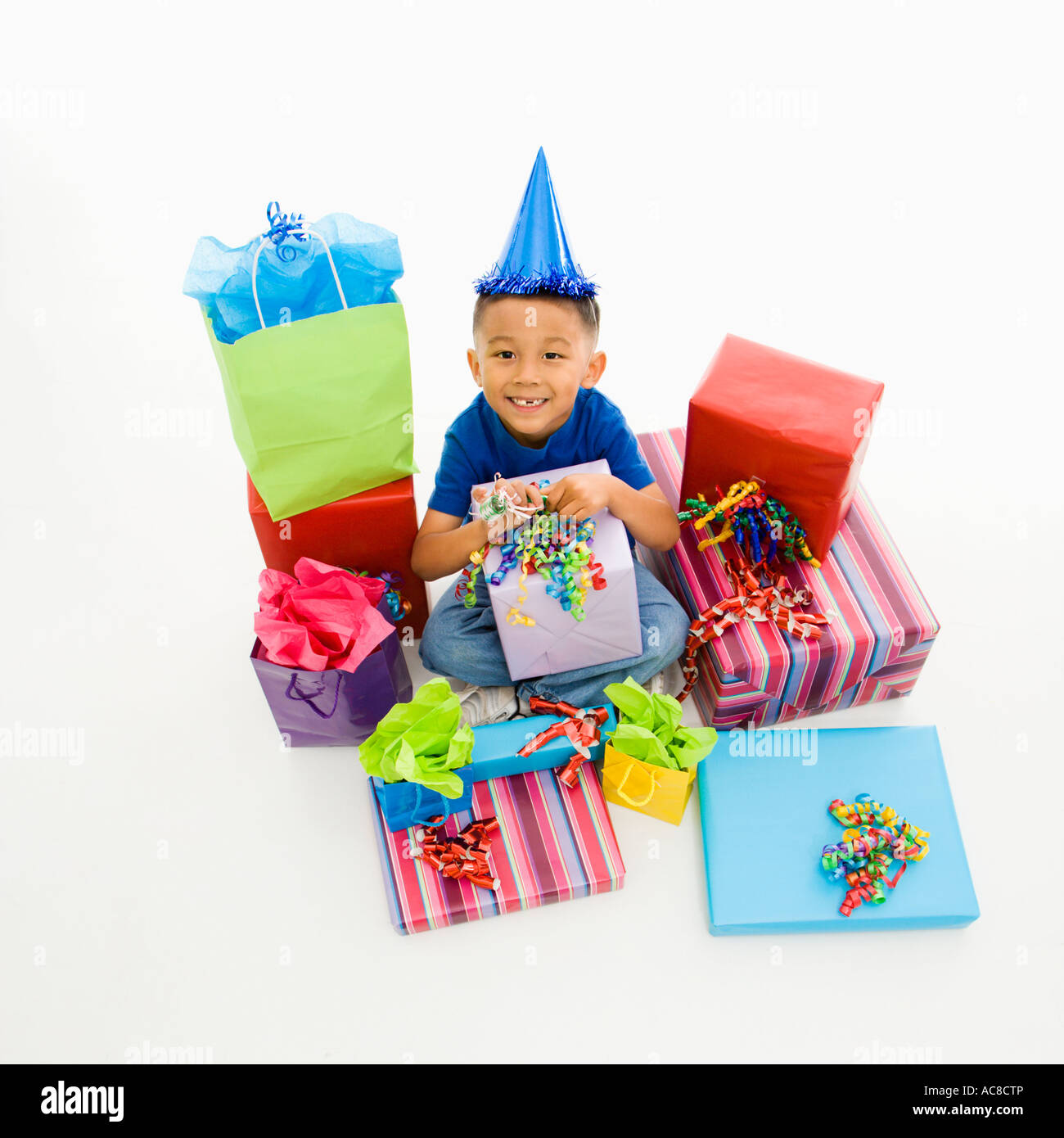 Asian boy wearing party hat sitting with pile of wrapped presents Stock ...