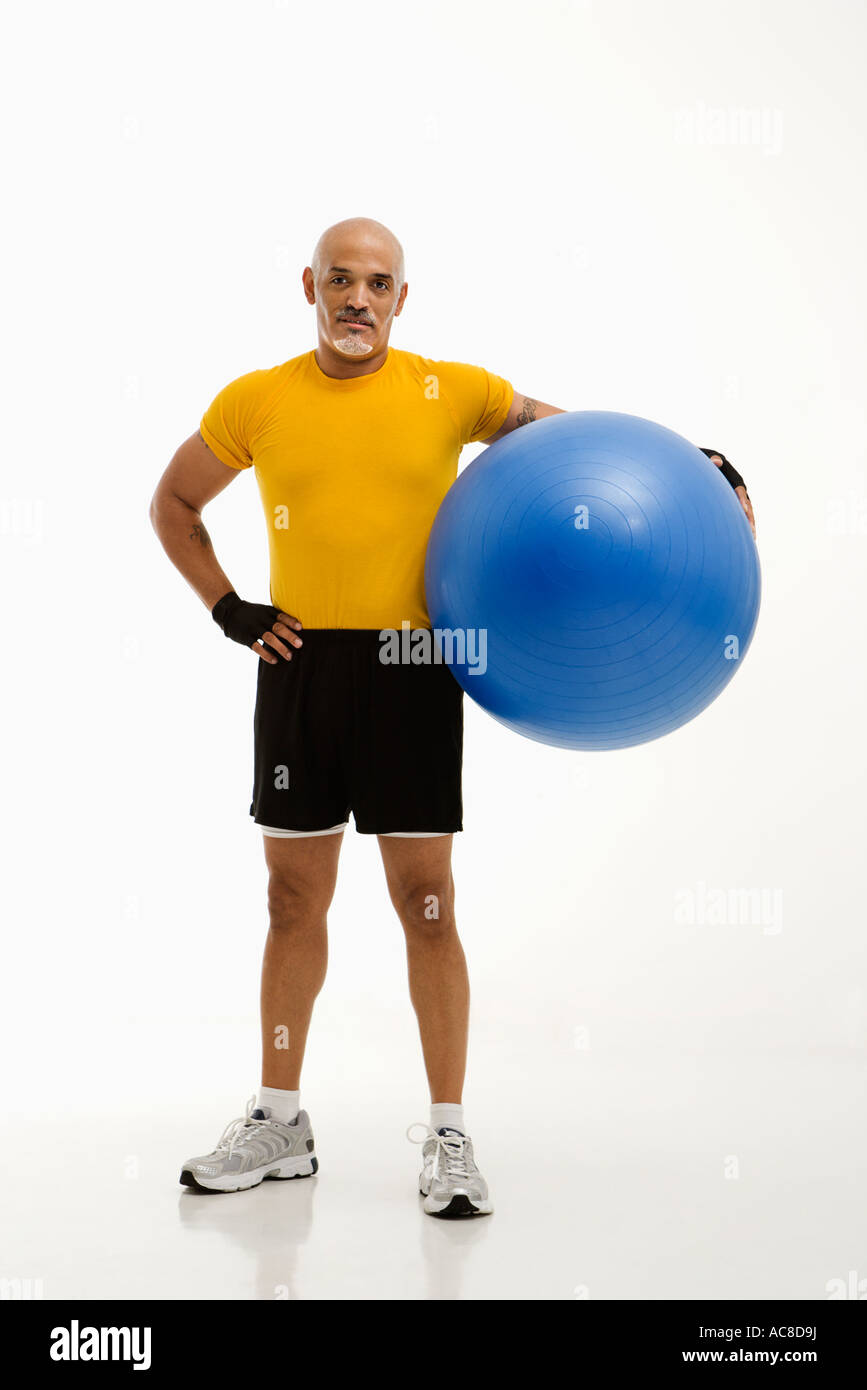 Mid adult multiethnic man standing and holding blue exercise ball ...
