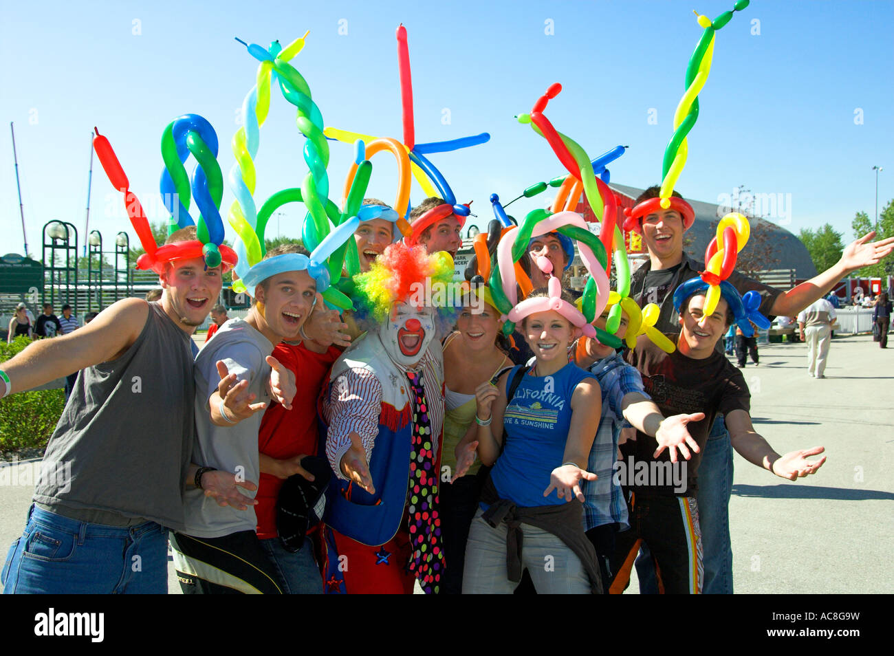 A clown in full costume playing to the camera with a group of teenagers ...