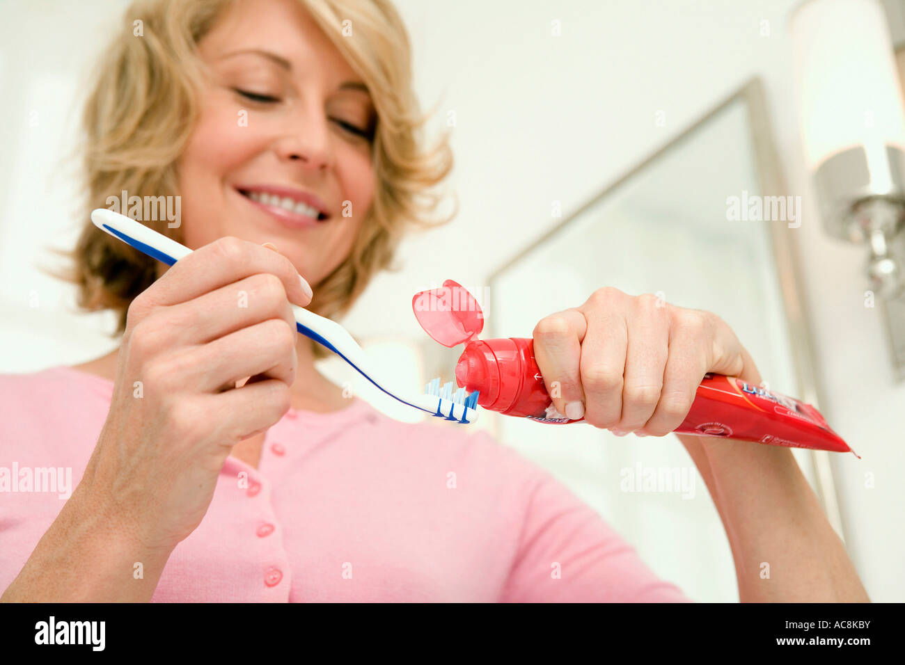 Low angle view of a mid adult woman putting toothpaste on a toothbrush ...
