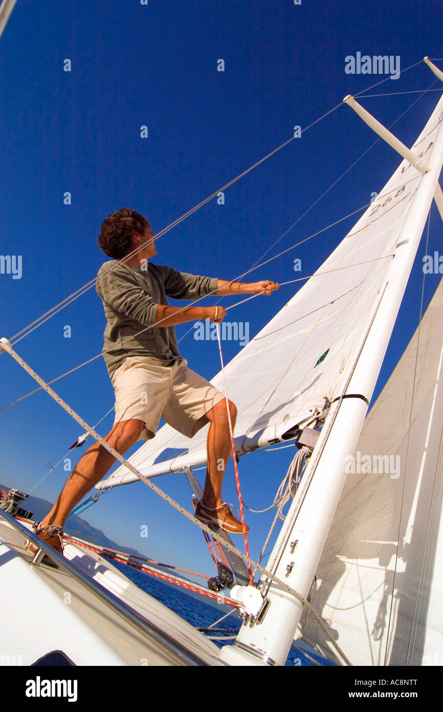 Low angle view of a young man standing on a sailboat and pulling a rope ...