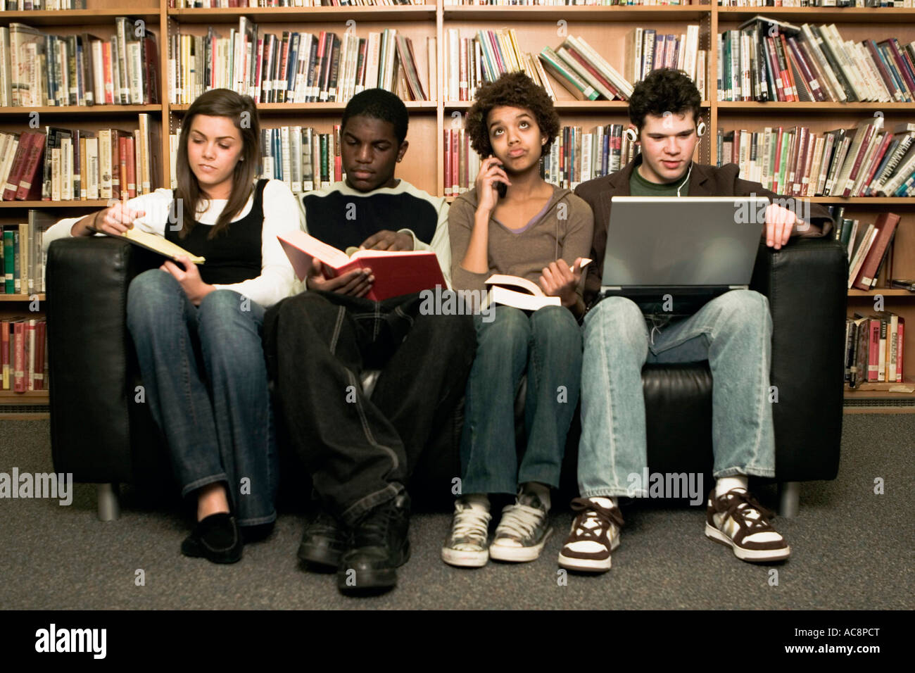 Four students sitting on a couch in a library Stock Photo - Alamy