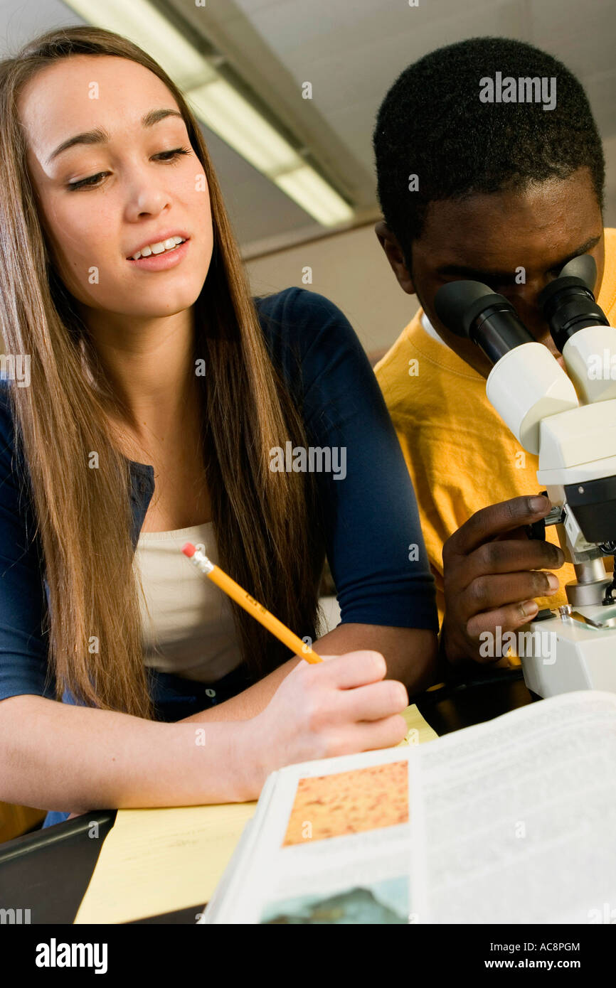 One student looking through a microscope with another student writing ...