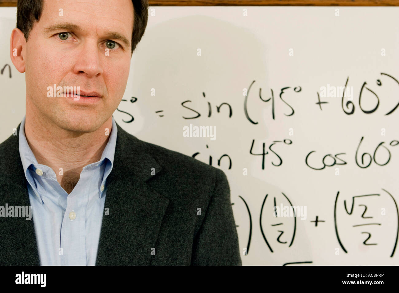 Portrait of a male teacher in front of a math equation on a whiteboard ...