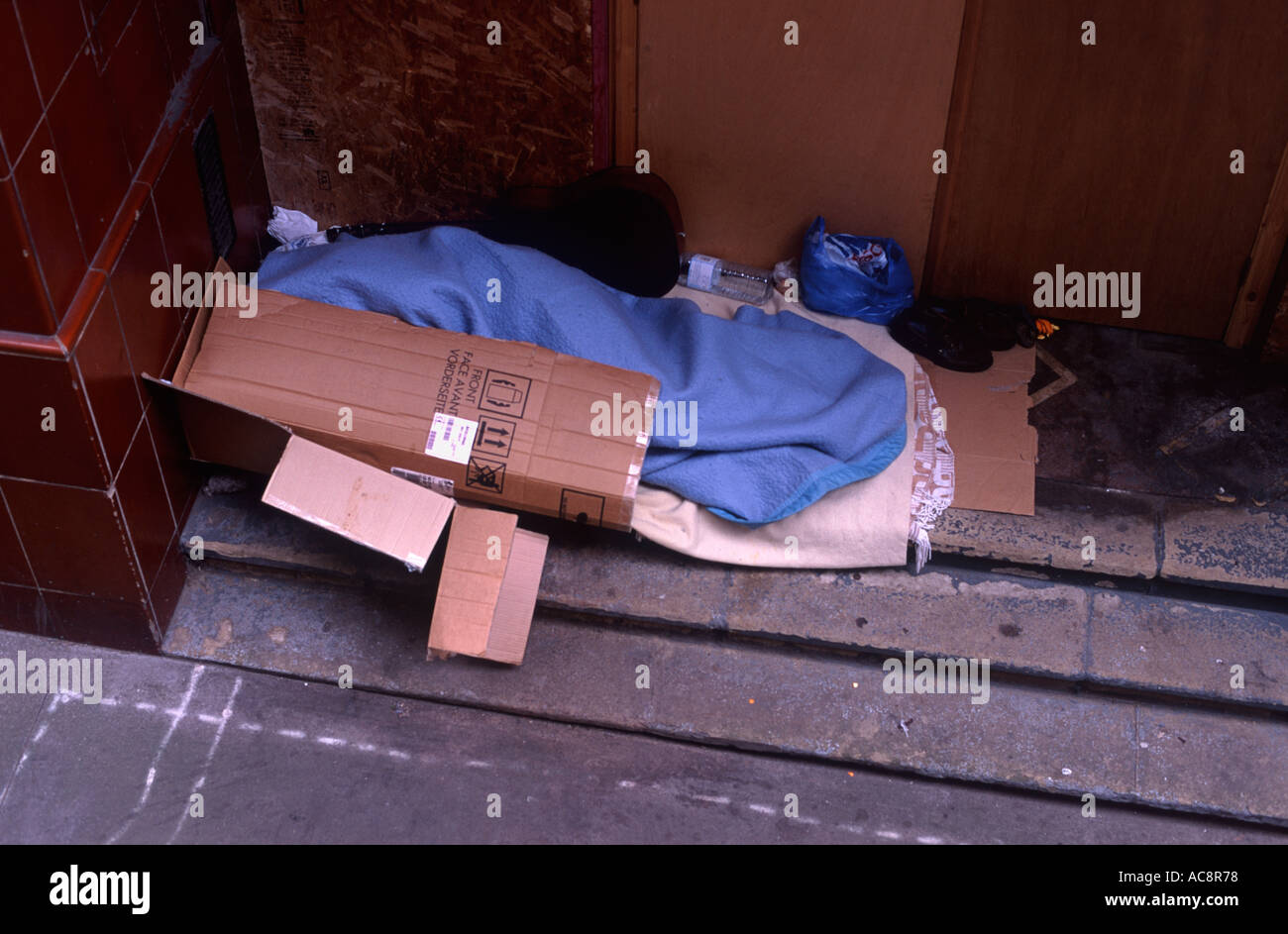 Homeless person sleeping under blankets and cardboard beside a building ...
