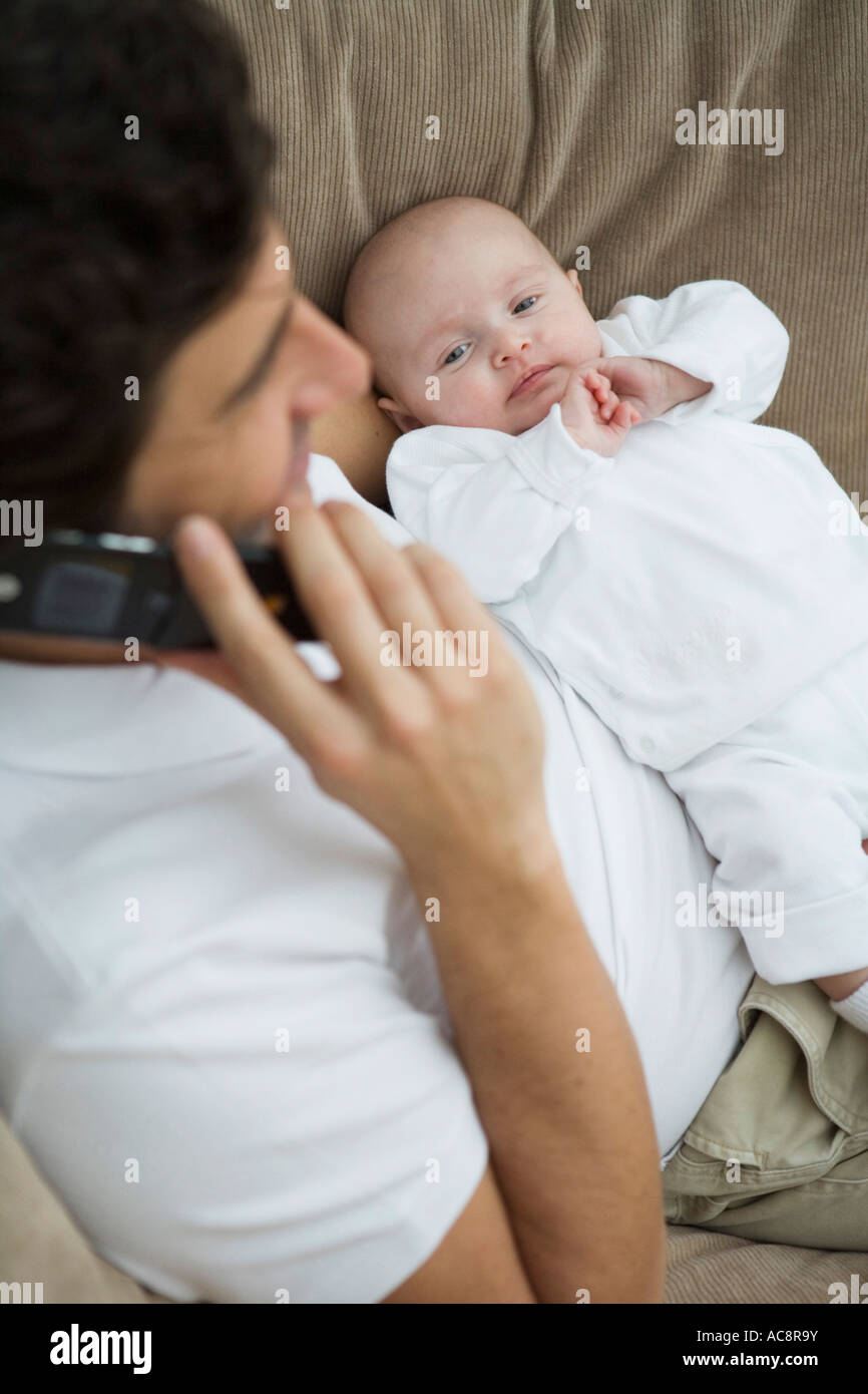 Mid adult man holding his baby while talking on a mobile phone Stock ...