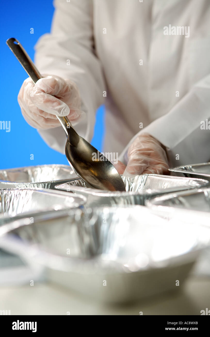 Food processing plant with aluminum trays being filled, blue background ...