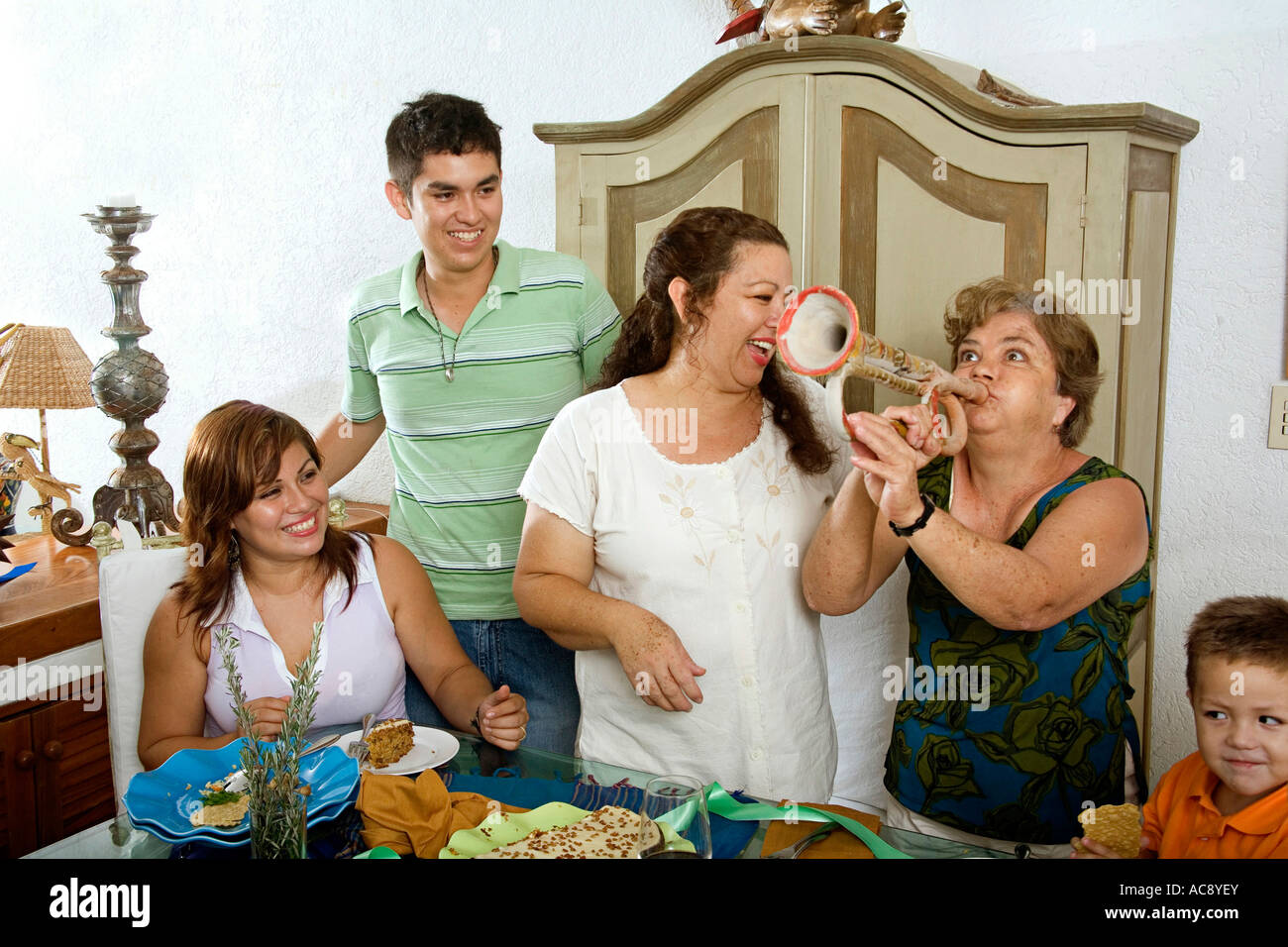 Mature woman playing a bugle with her family at a dining table Stock ...