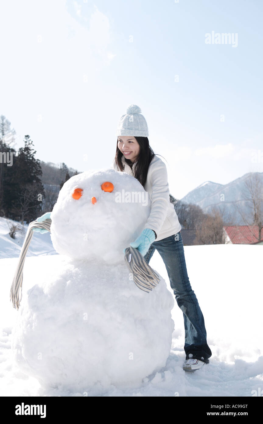 Young woman putting scarf on snowman Stock Photo - Alamy