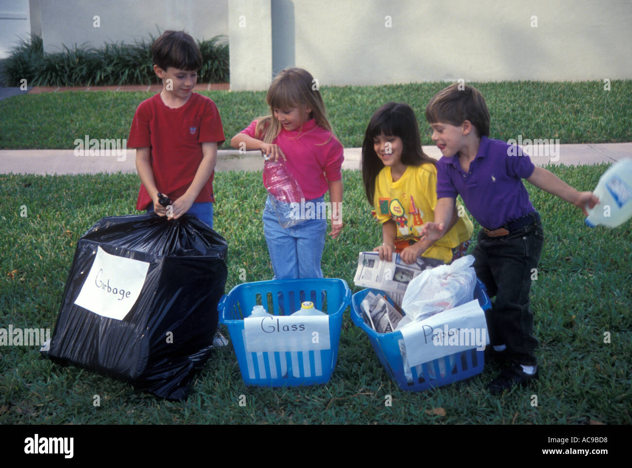 Four young children working to recycle glass and paper while taking out ...